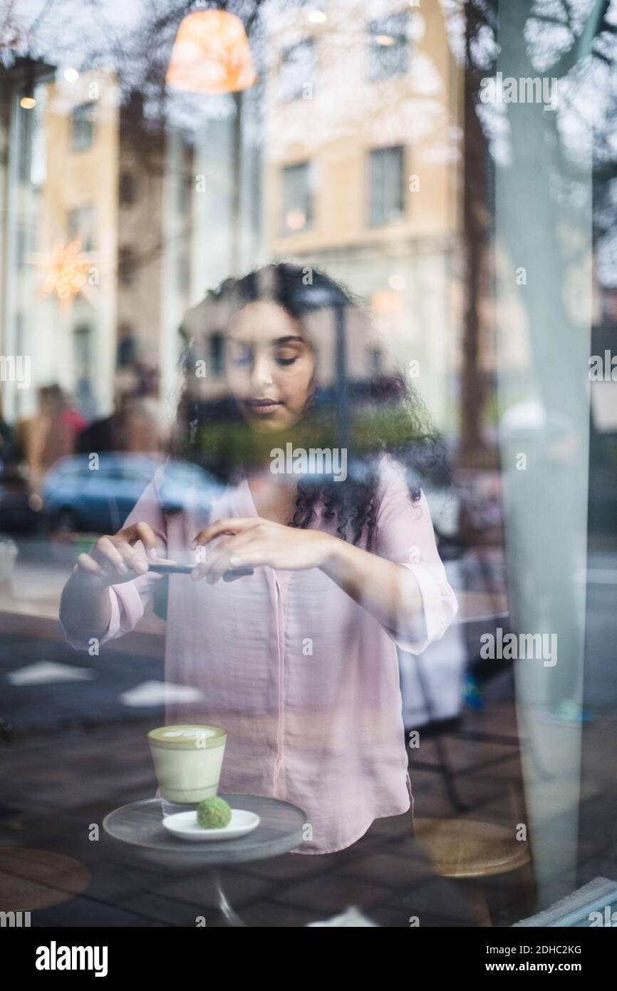 Young female influencer photographing tea and snack on table through ...