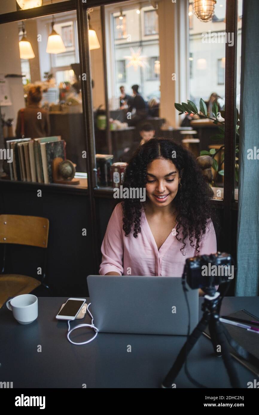 Confident young female influencer using laptop while vlogging at ...