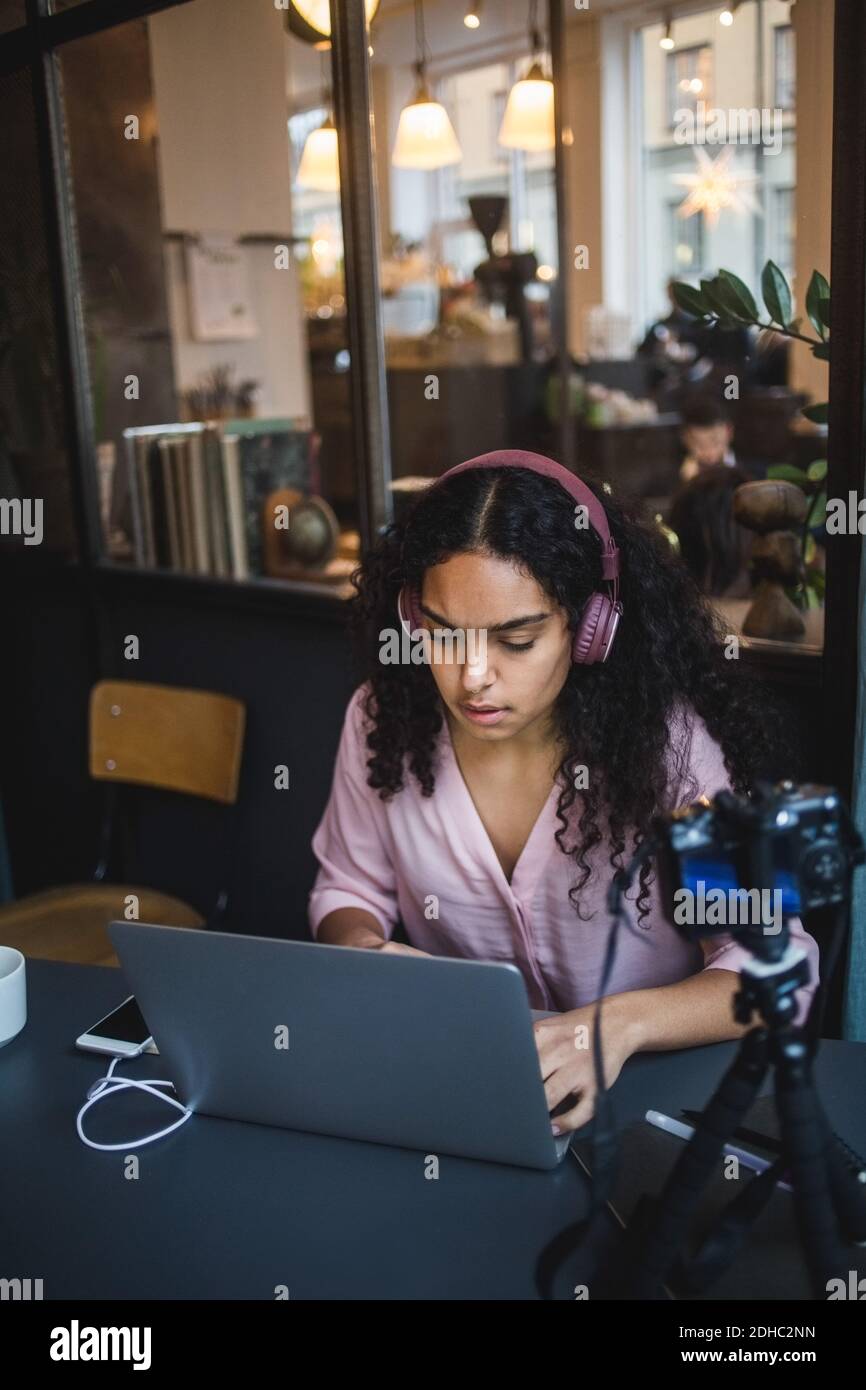 Confident young female influencer using laptop while vlogging at desk ...