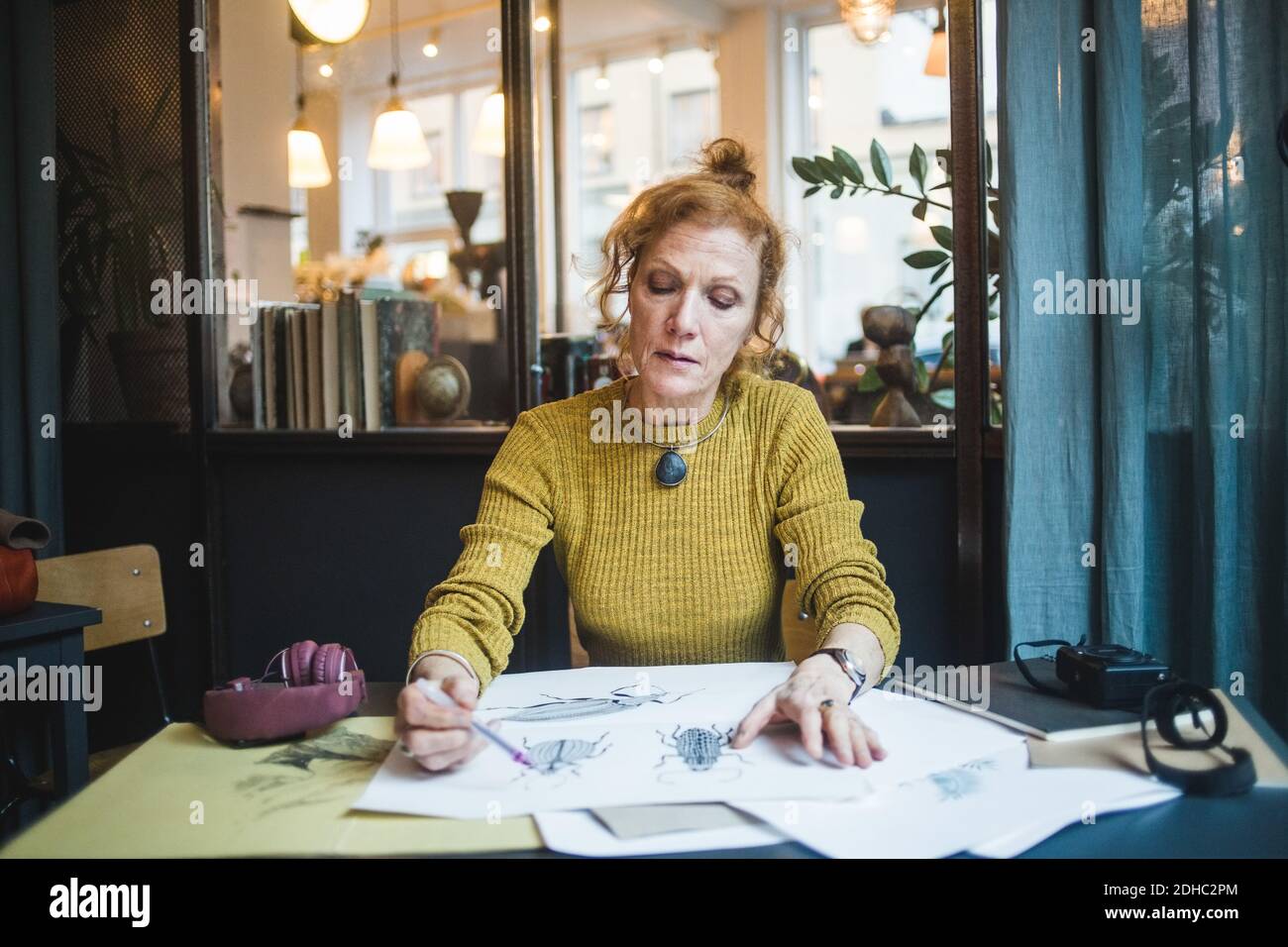 Confident mature female illustrator drawing on paper at desk in ...