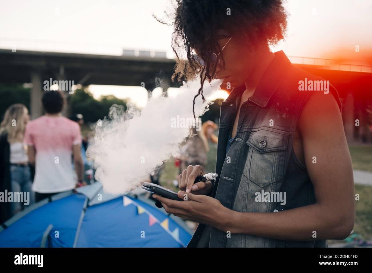 Side view of young man smoking while using mobile phone at music event ...