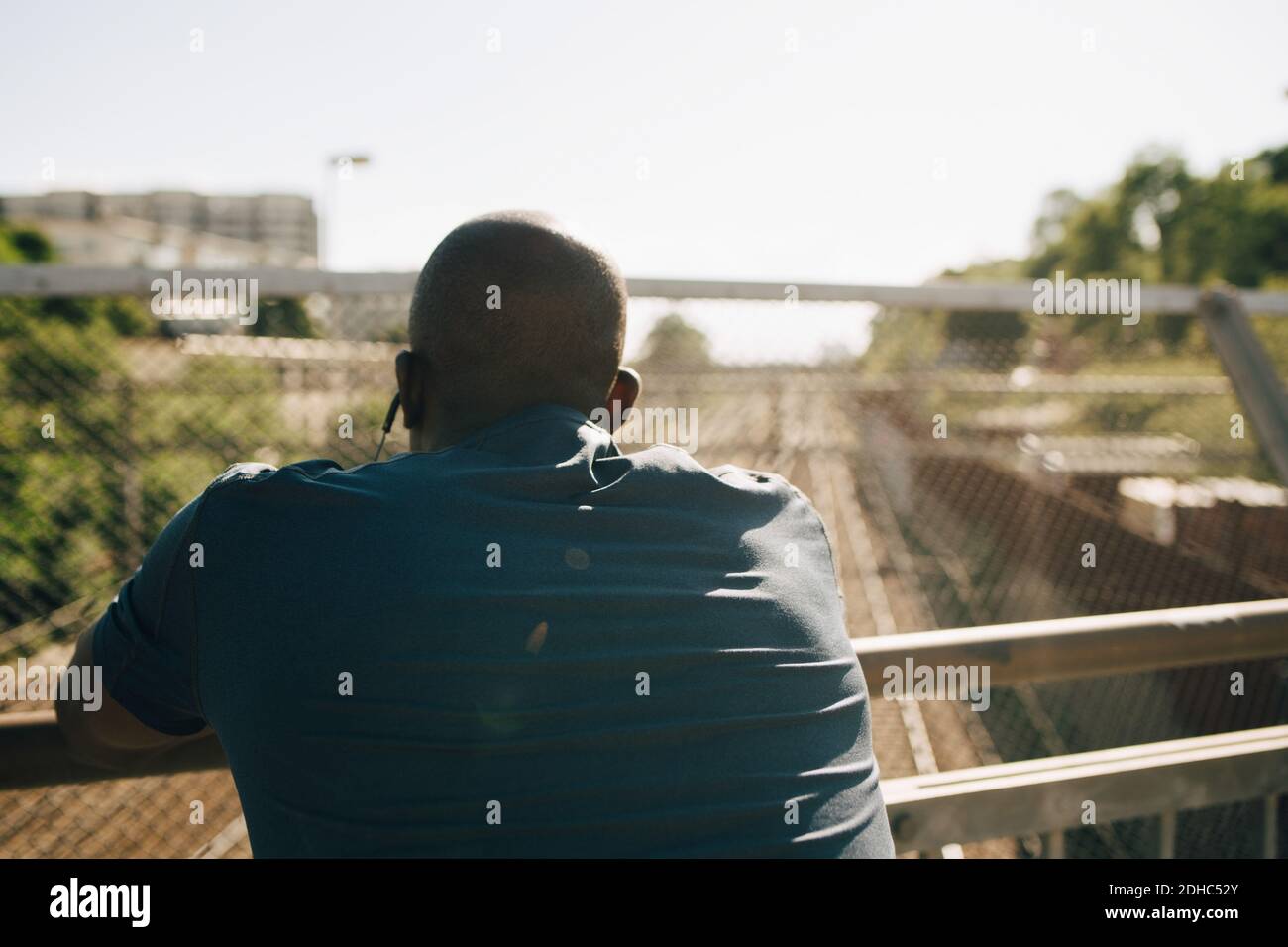 Rear view of exhausted male athlete leaning on railing during sunny day ...