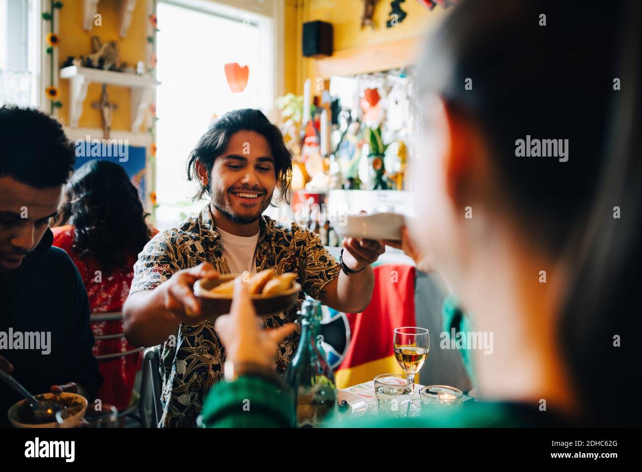 Smiling young man giving food to woman while sitting by friend at table ...