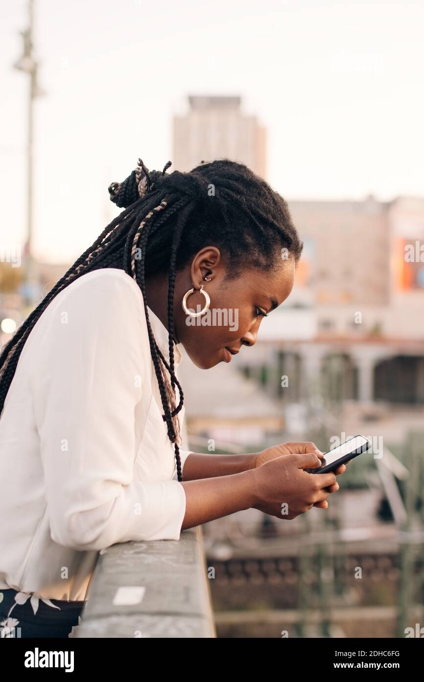 Side view of young woman text messaging through mobile phone while ...