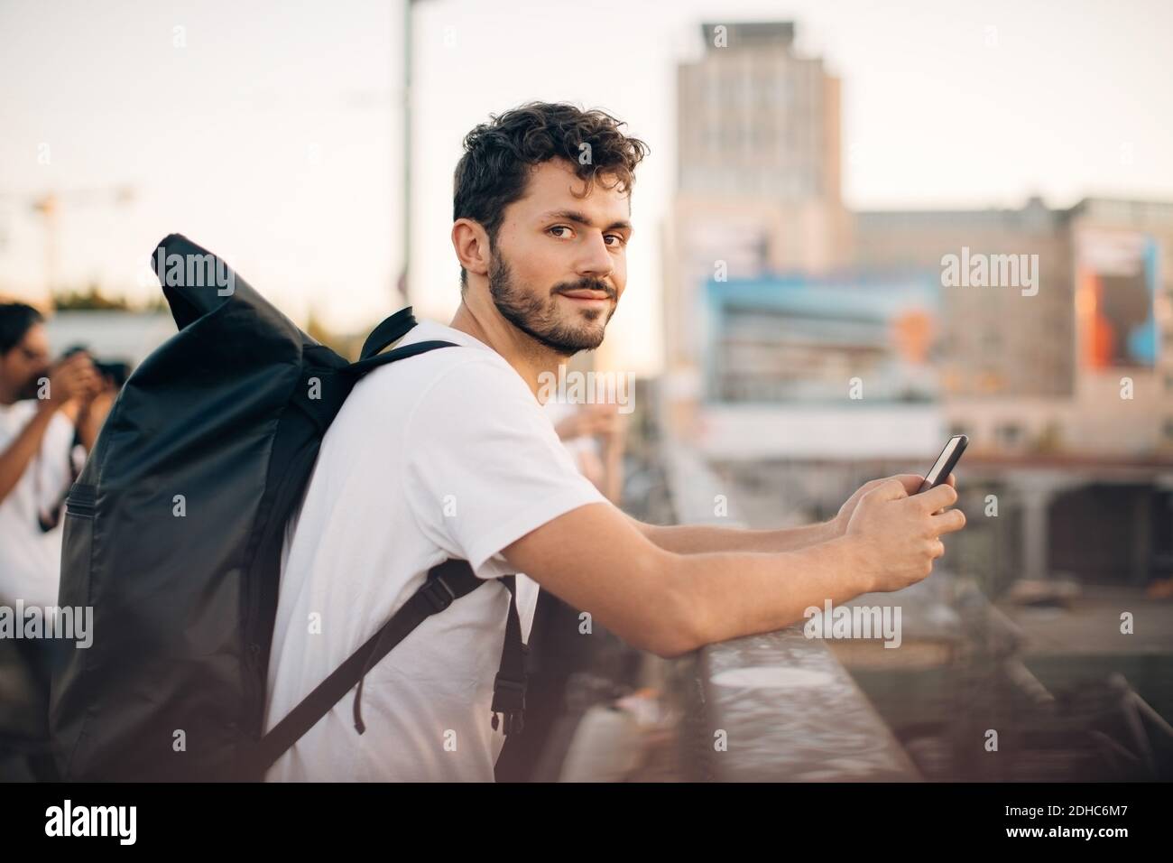 Side view portrait of young man holding mobile phone while leaning on ...