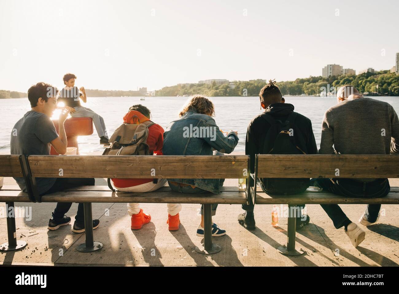 Friends eating take out food while sitting side by side on bench in ...