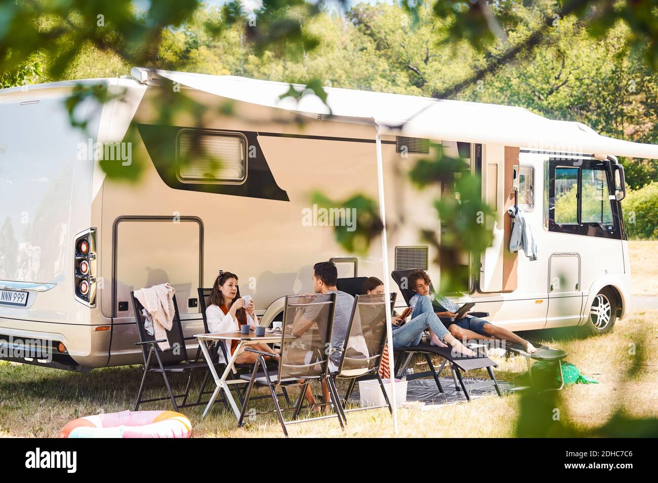 Family relaxing on chairs outside camper van at campsite during summer ...