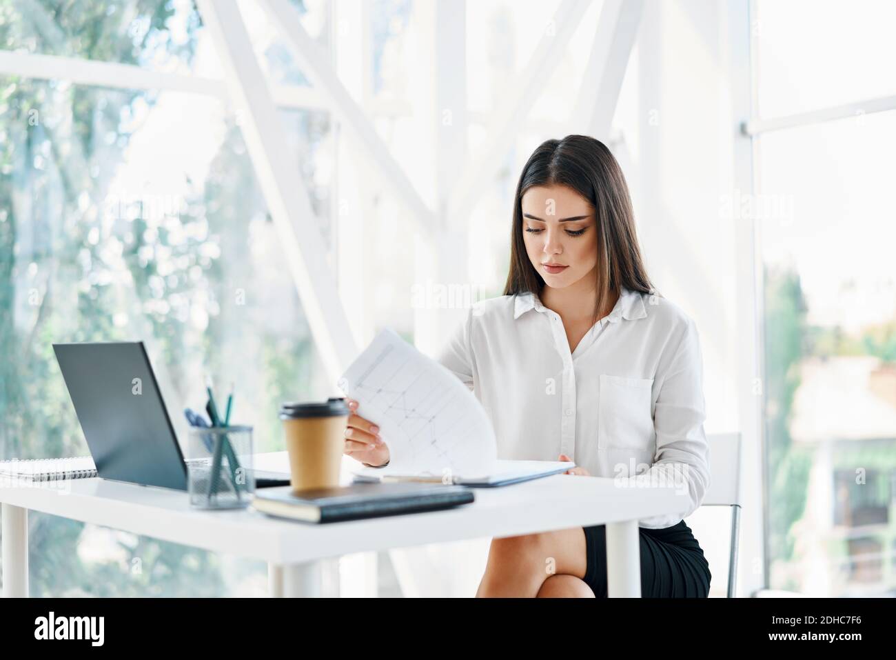 Pretty businesswoman sitting at workplace and reading documents in her ...
