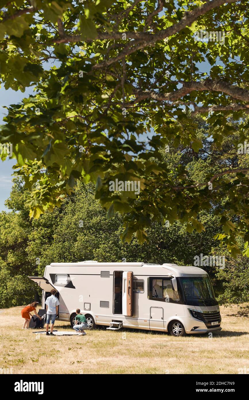 Mother and children unloading camper trailer parked against trees at ...