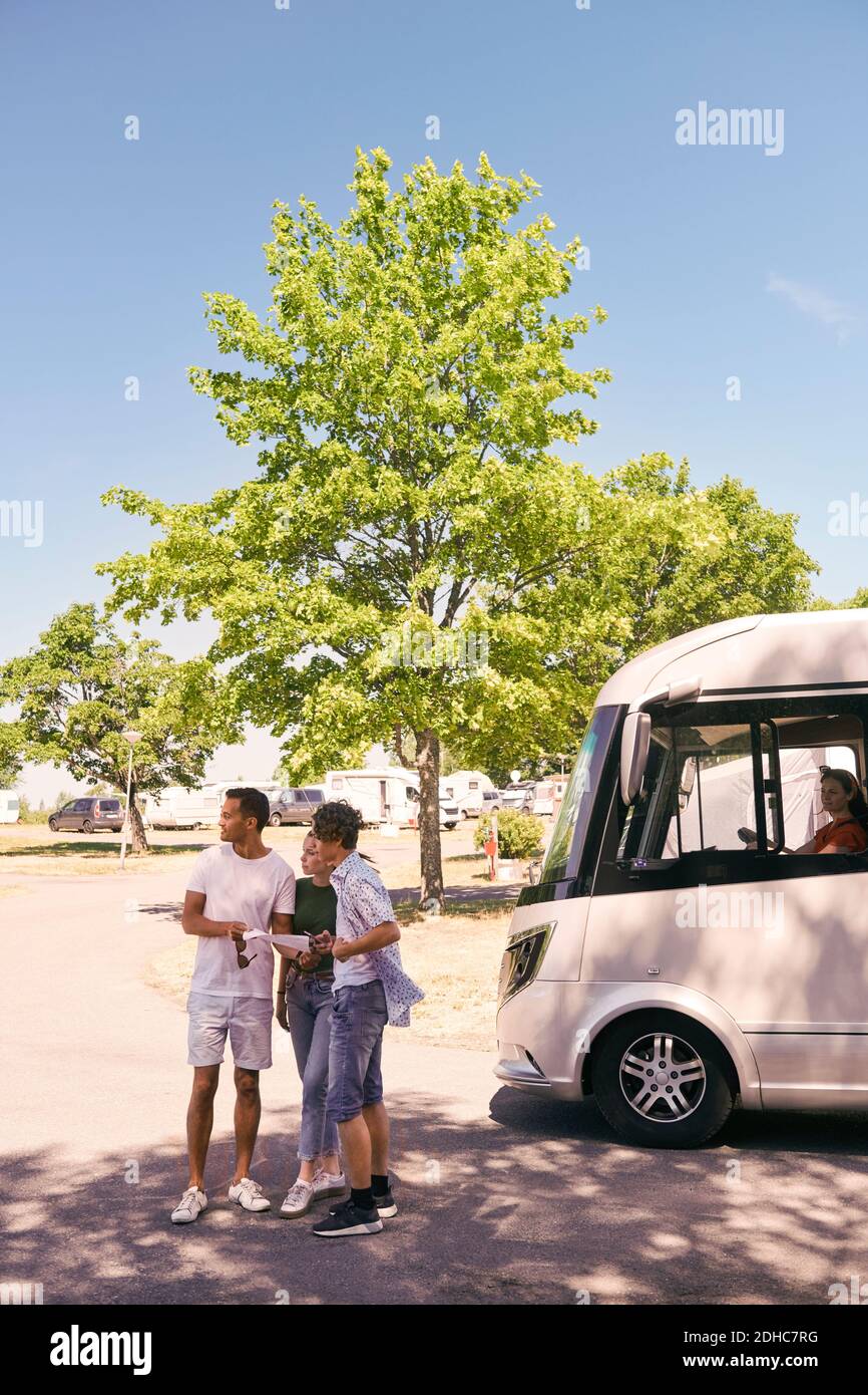 Father and children reading map while woman sitting in camper trailer ...
