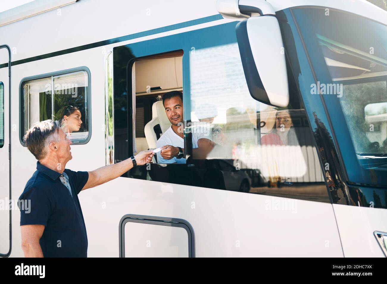 Senior man giving ticket to male in motor home while entering at ...