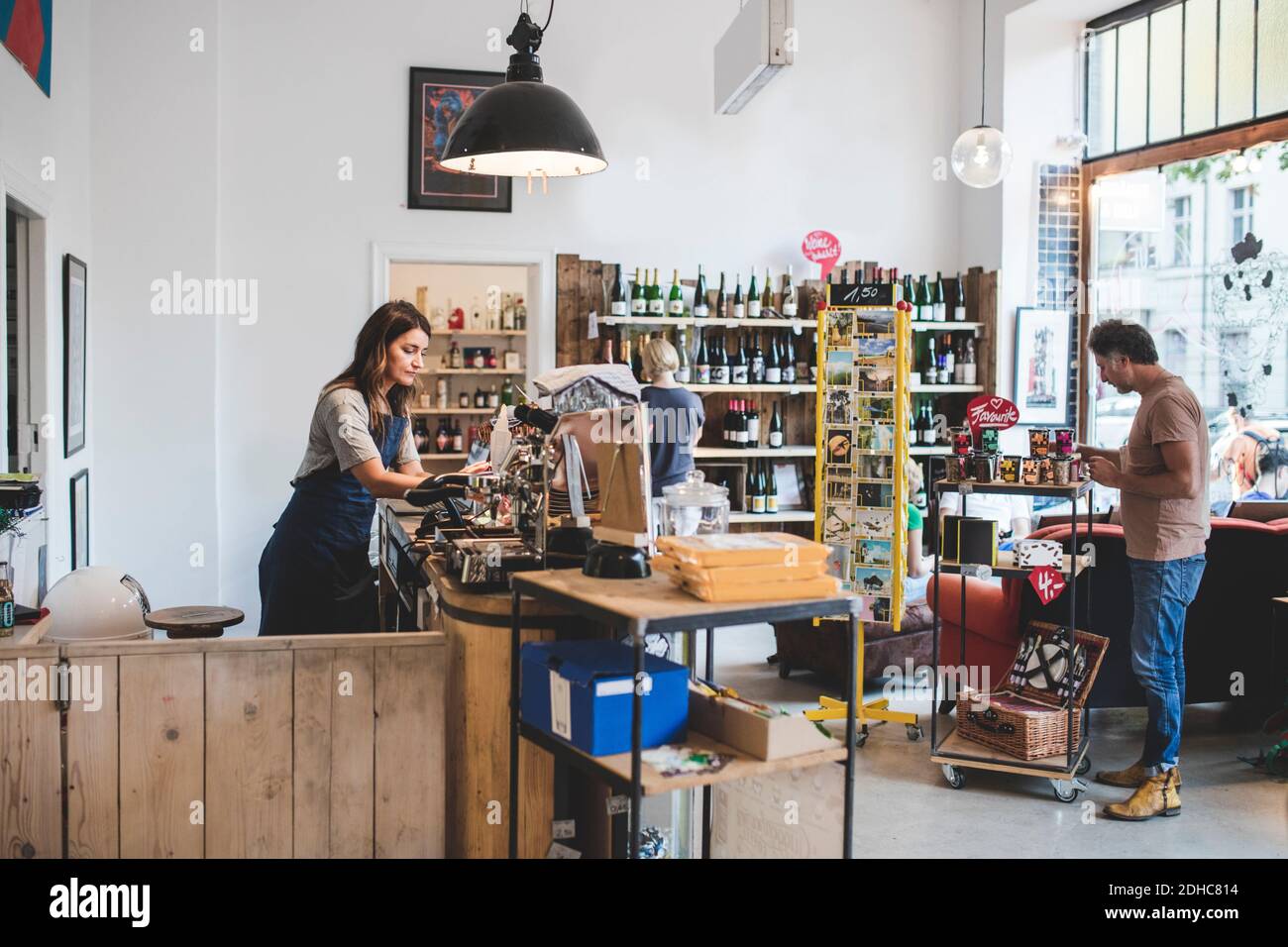 Female sales clerk working at checkout counter while customers shopping ...