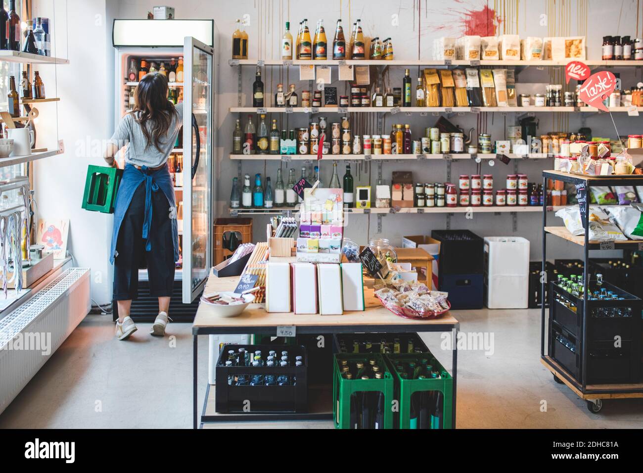 Rear view of female employee arranging bottles in refrigerator at deli ...