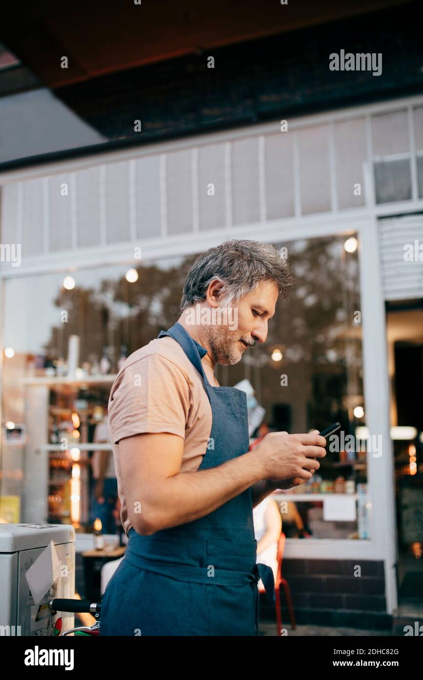 Side view of male owner using mobile phone outside deli Stock Photo - Alamy