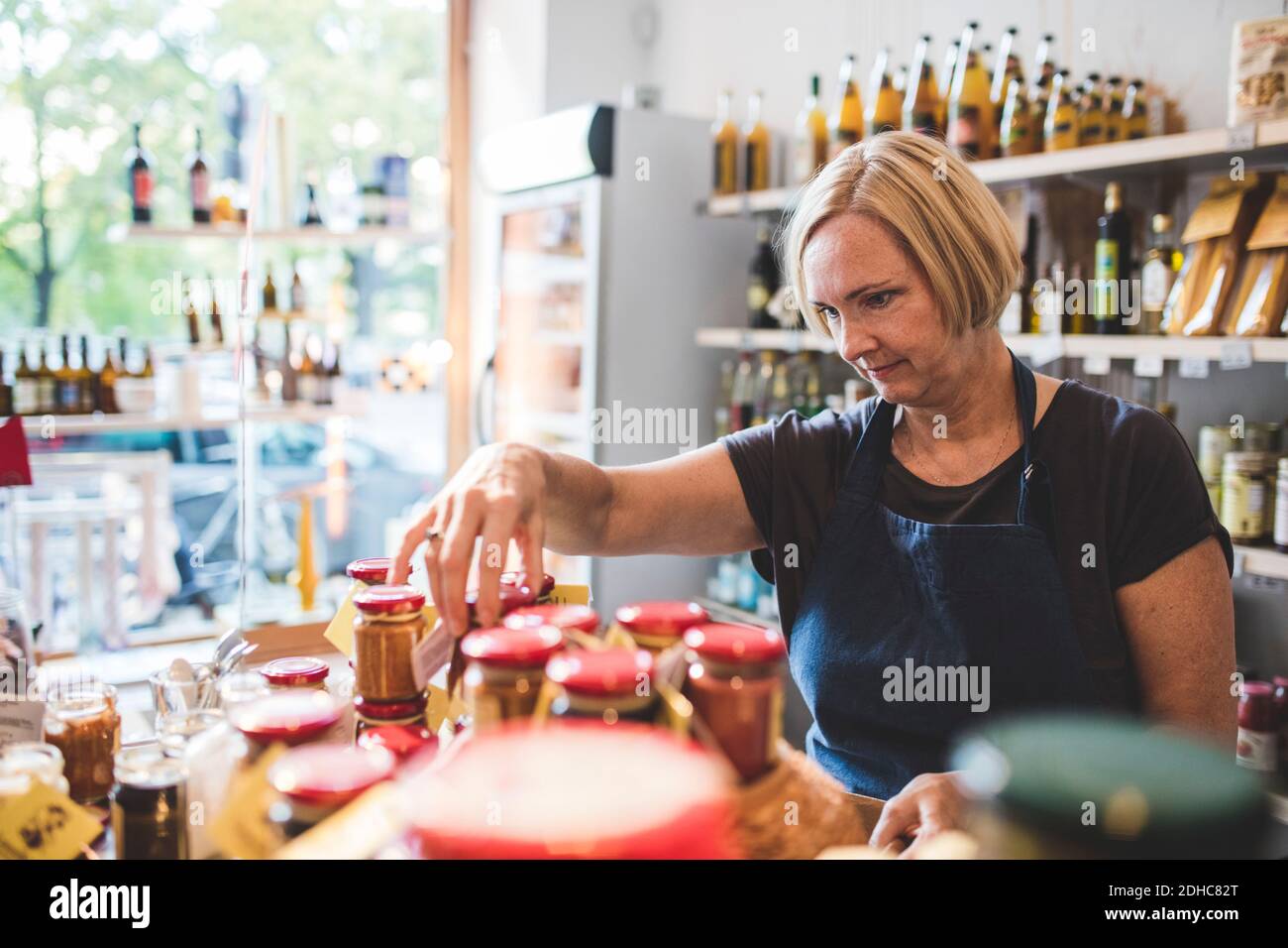 Mature female employee arranging jars in deli Stock Photo - Alamy