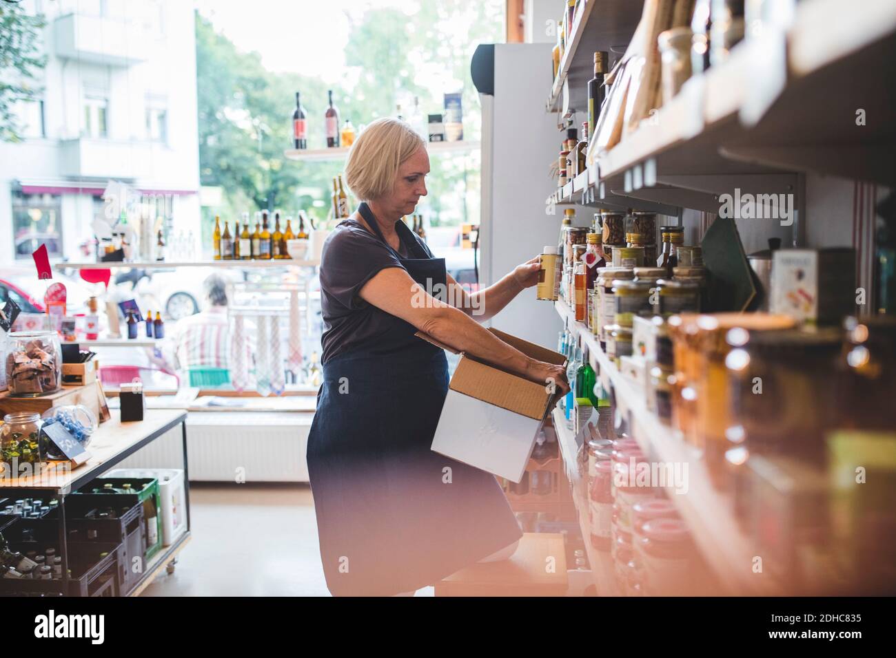 Mature female employee arranging food products on shelf in deli Stock ...