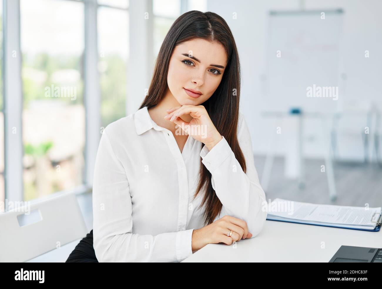 Portrait of smiling pretty young businesswoman sitting on workplace at ...