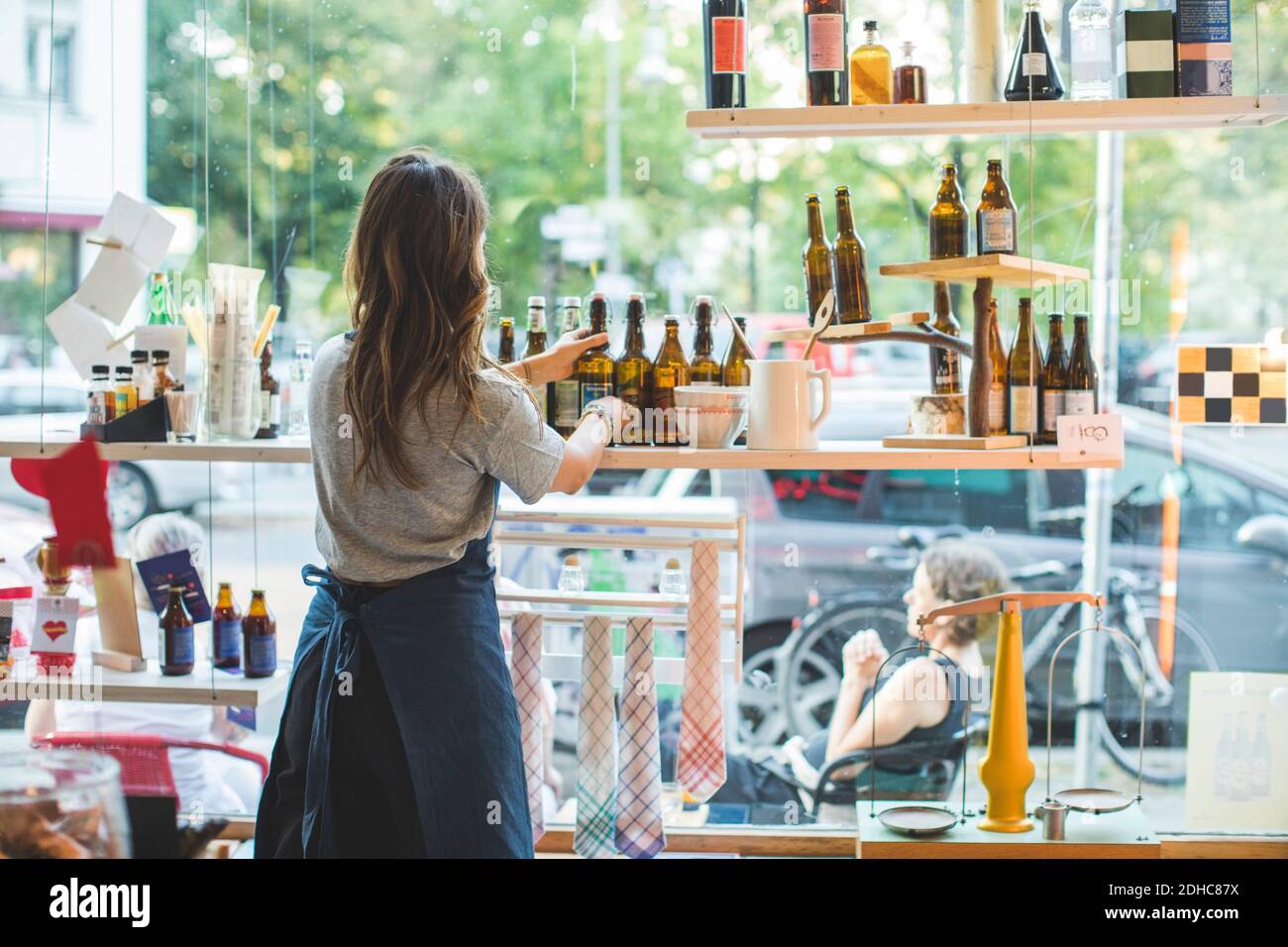 Rear view of female employee arranging bottles on shelf in deli Stock ...