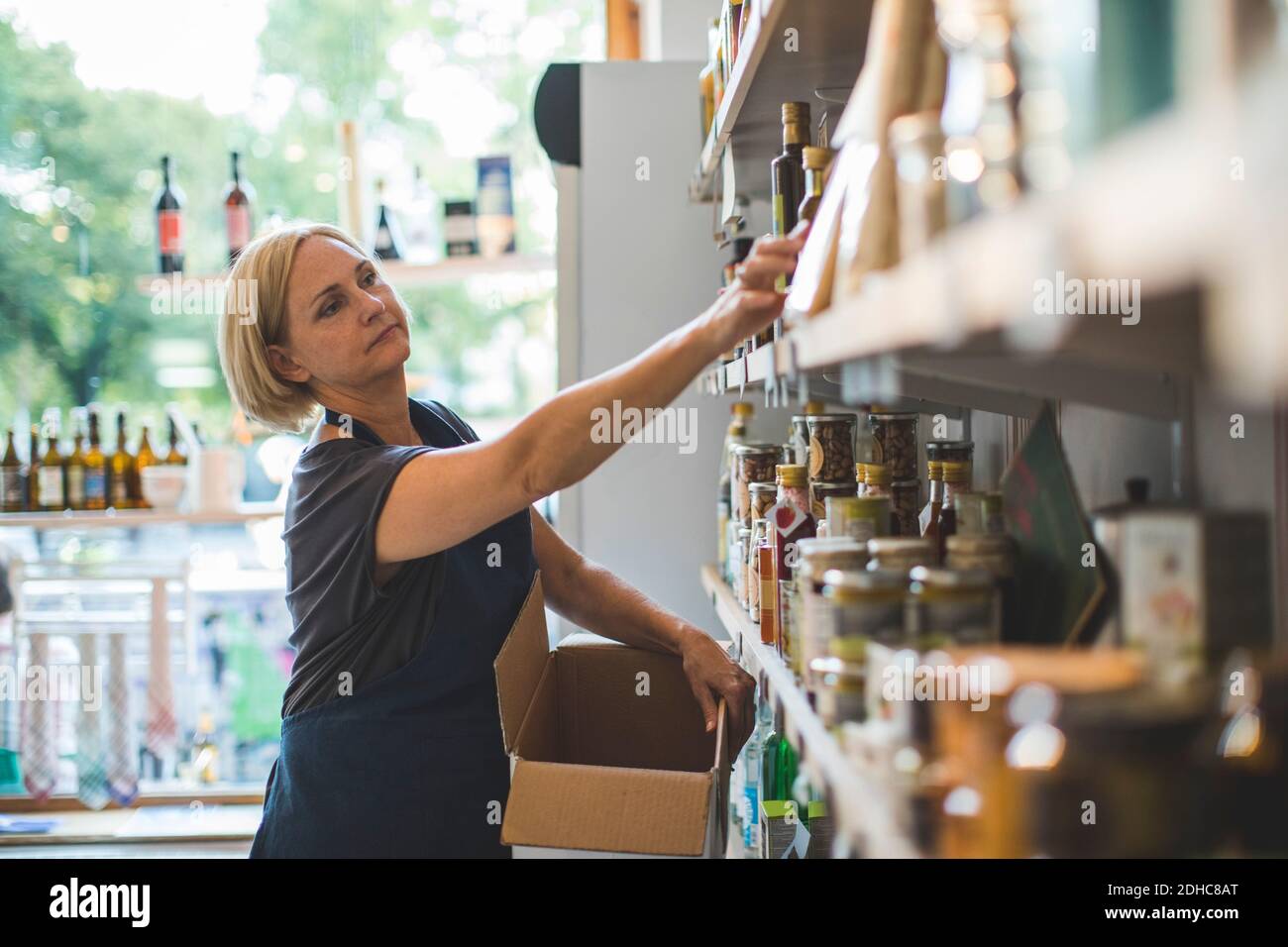 Mature female employee arranging bottles on shelf in deli Stock Photo ...