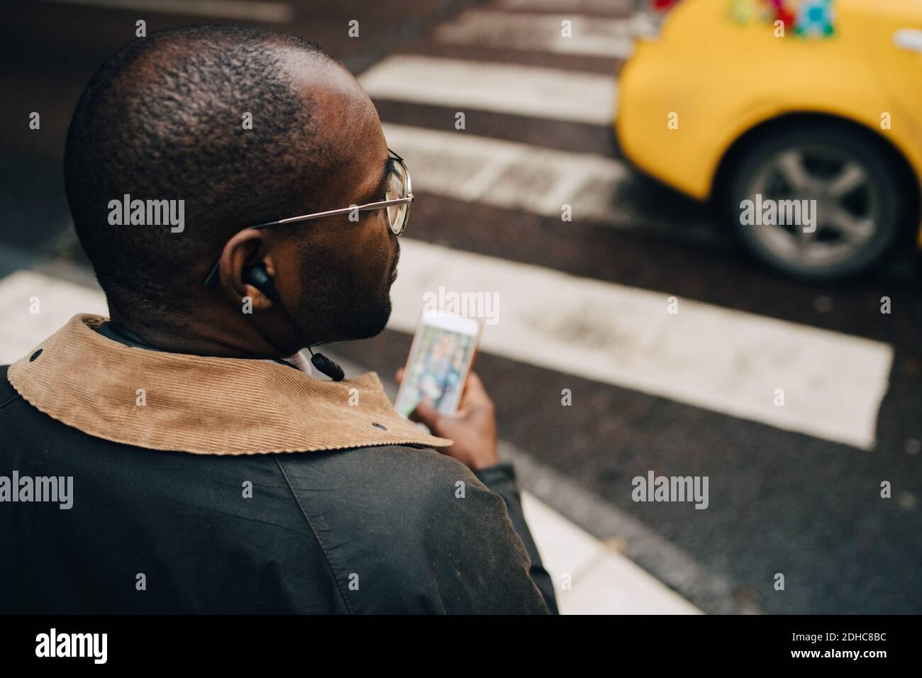 Rear view of businessman using mobile phone while crossing road in city ...