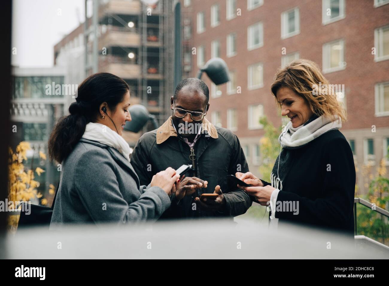 Colleagues using mobile phones while standing against building in city ...