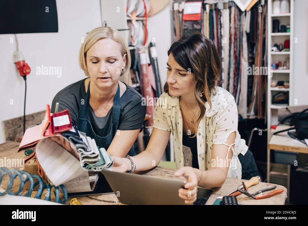 Female upholstery workers discussing over fabric swatch in workshop ...