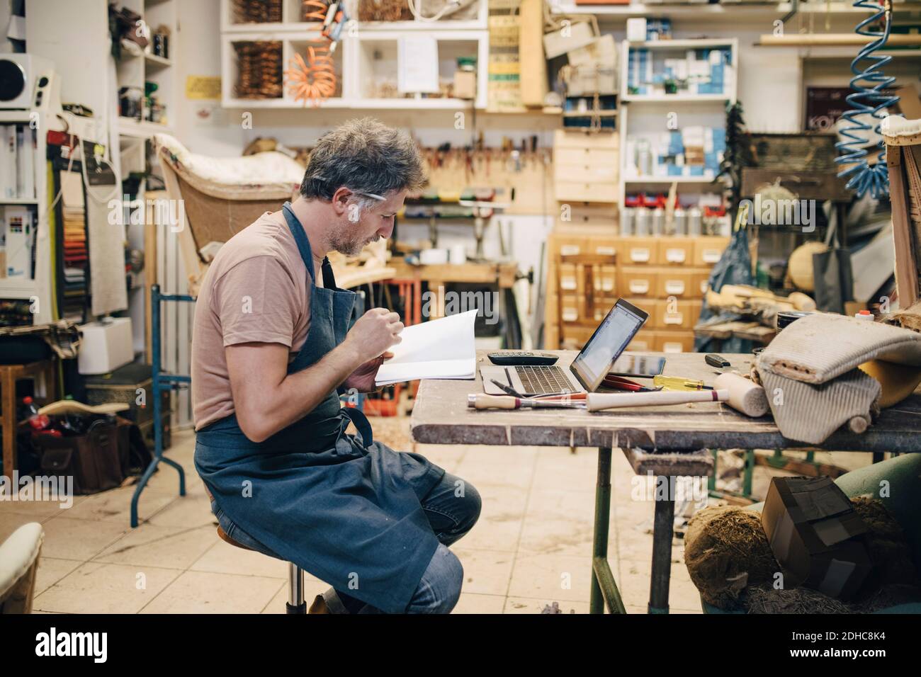 Side view of male upholstery worker reading book while sitting at ...
