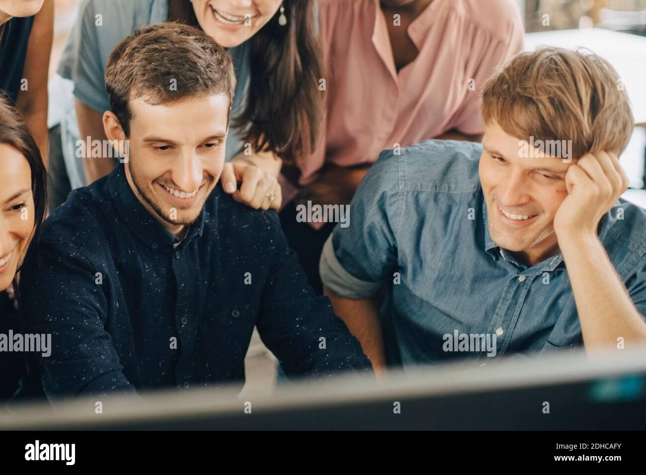 Smiling creative business people looking at computer monitor during ...