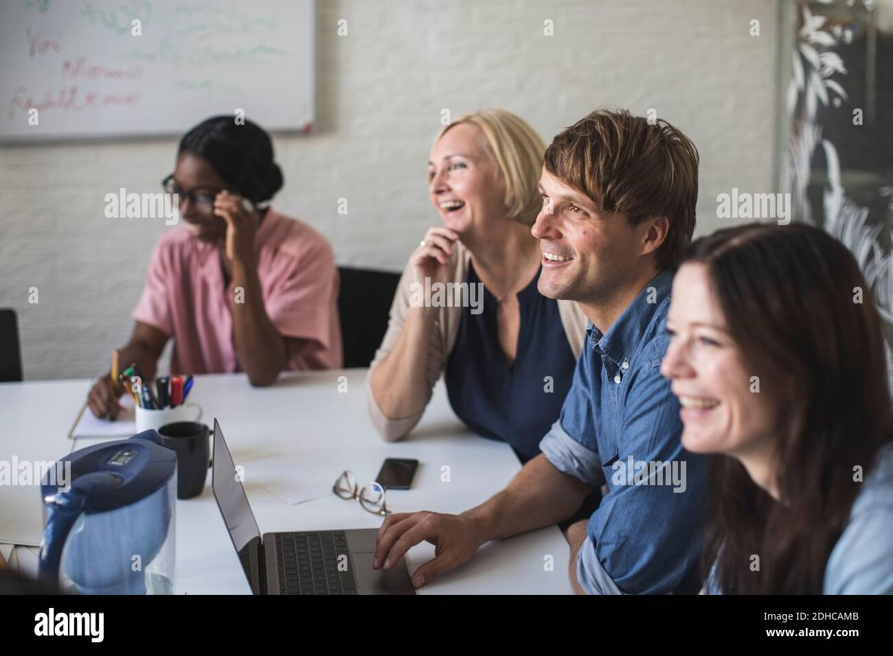 Creative business people smiling while sitting at conference table in ...