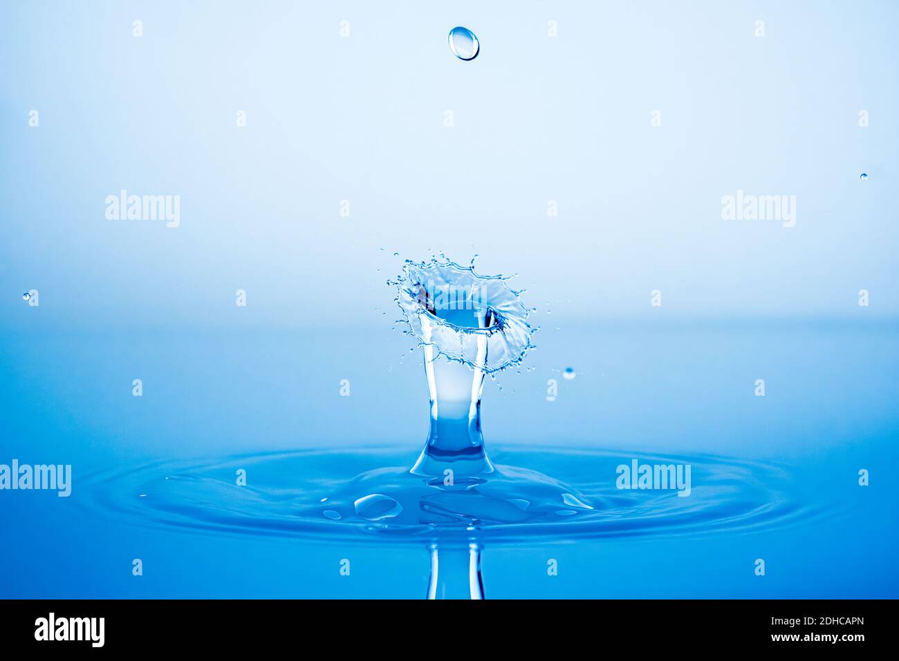 Water drop splashing into blue water surface Stock Photo - Alamy