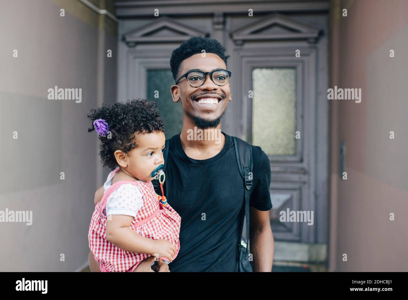 Happy father looking away while carrying daughter against closed door ...