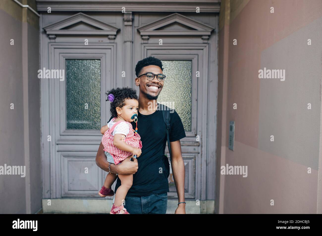 Smiling father looking away while carrying daughter against closed door ...
