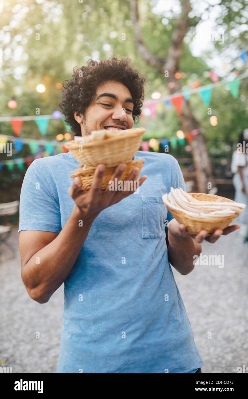 Smiling young man carrying food in bowls during dinner party in ...