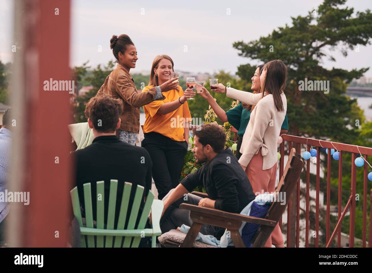 Female friends toasting drinks while men sitting on chairs during party ...