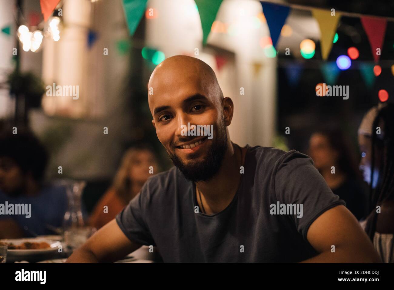 Portrait of smiling young man with shaved head sitting in backyard ...