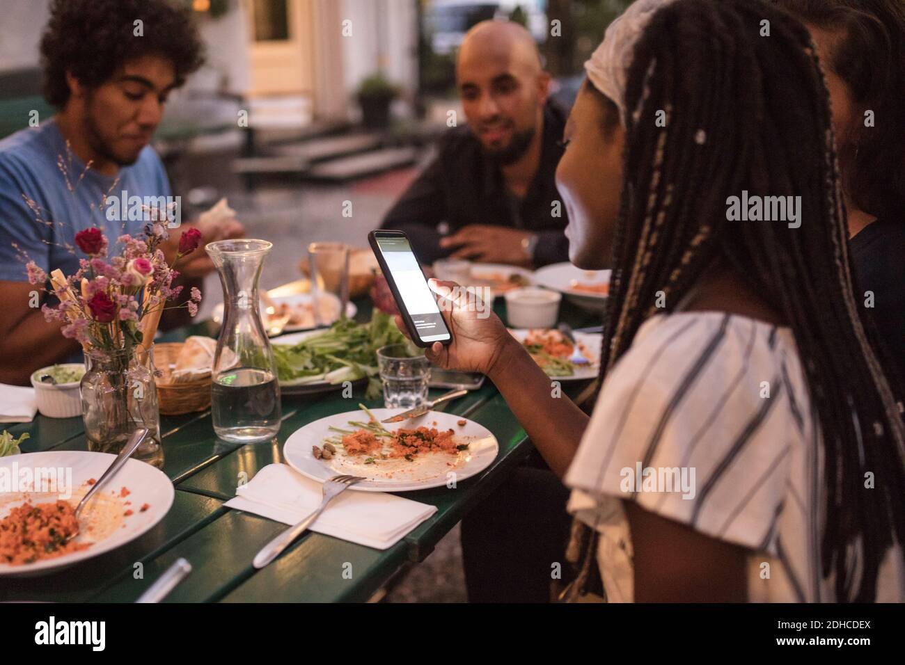 Young woman using smart phone while having dinner with friends during ...