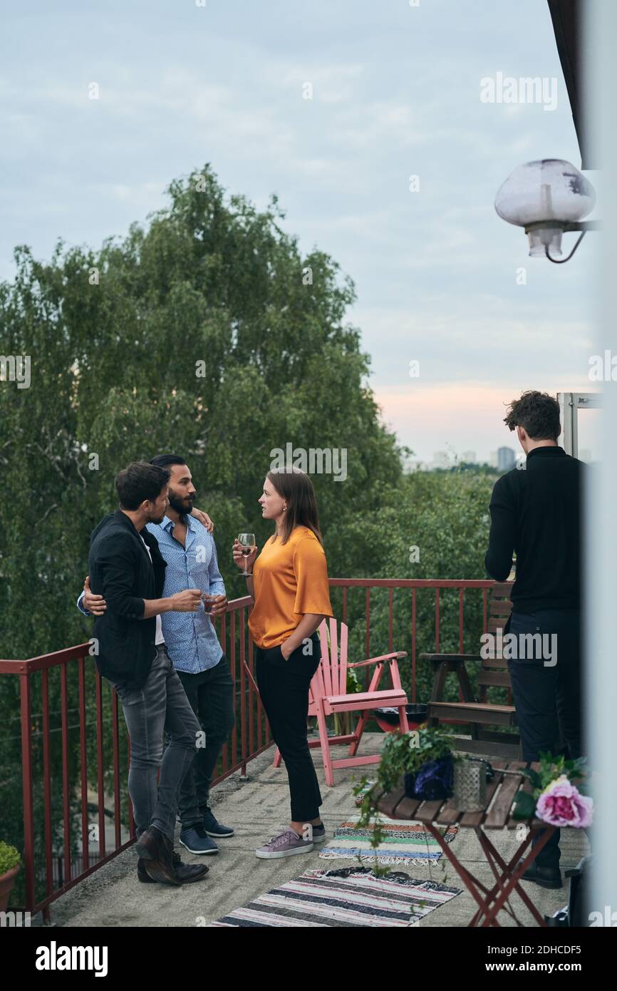 Full length of friends talking while standing on terrace during social ...