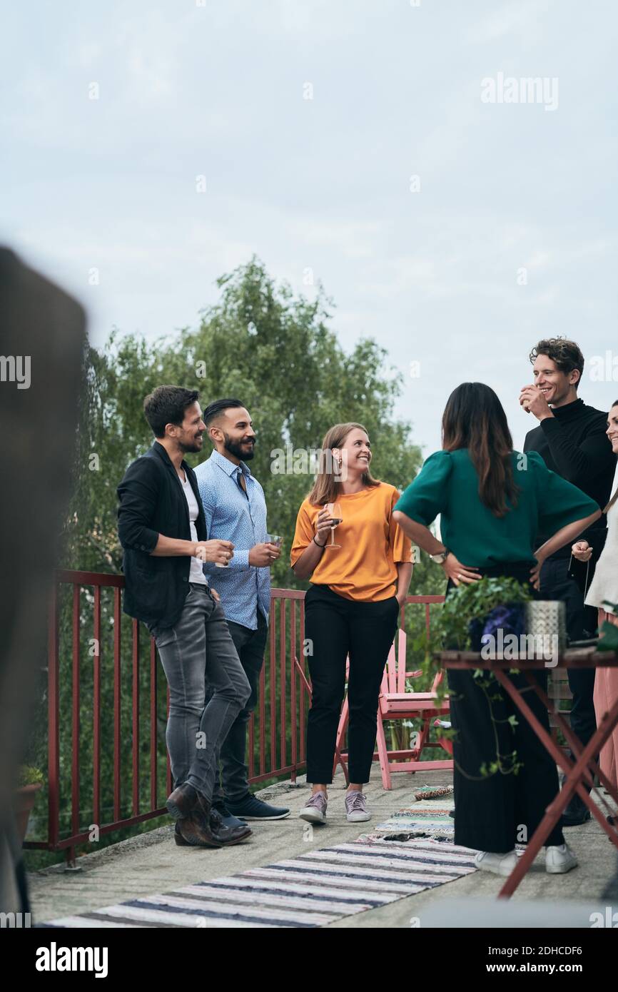 Happy friends talking while standing on terrace during social gathering ...