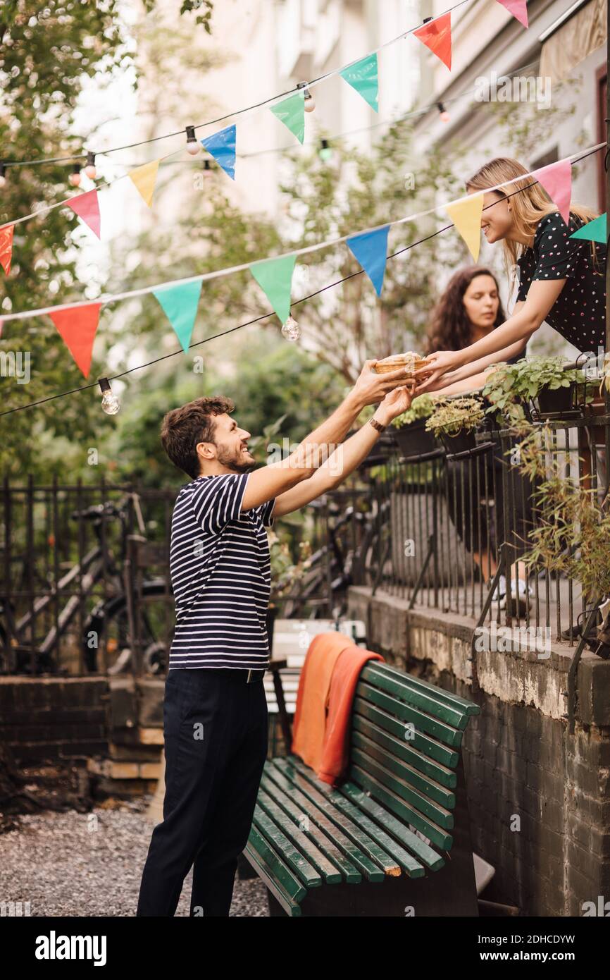 Young woman giving food to smiling male friend from balcony during ...