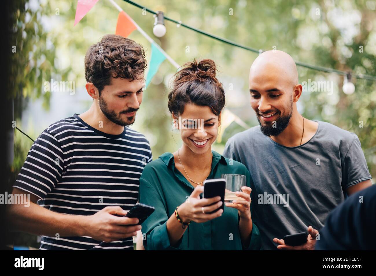 Happy young woman showing mobile phone to male friends while standing ...