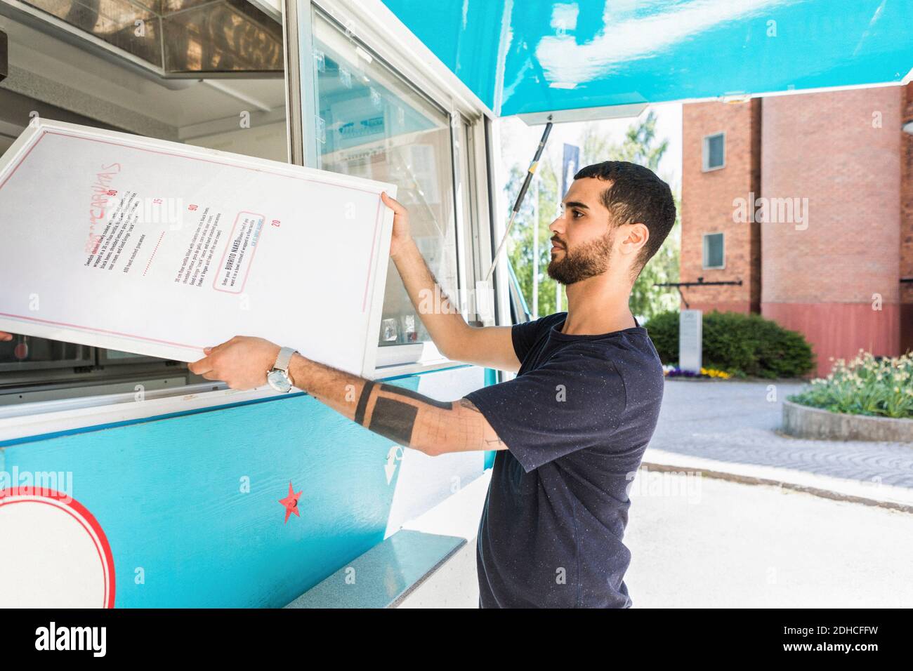 Side view of confident young male salesman holding menu placard at food ...
