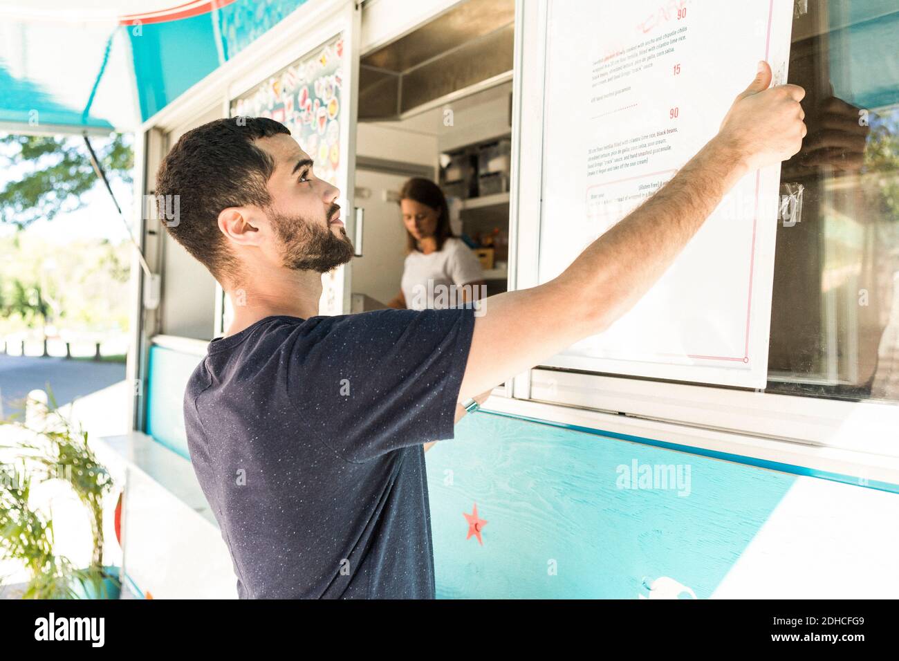 Confident young male salesman positioning menu placard on food truck ...