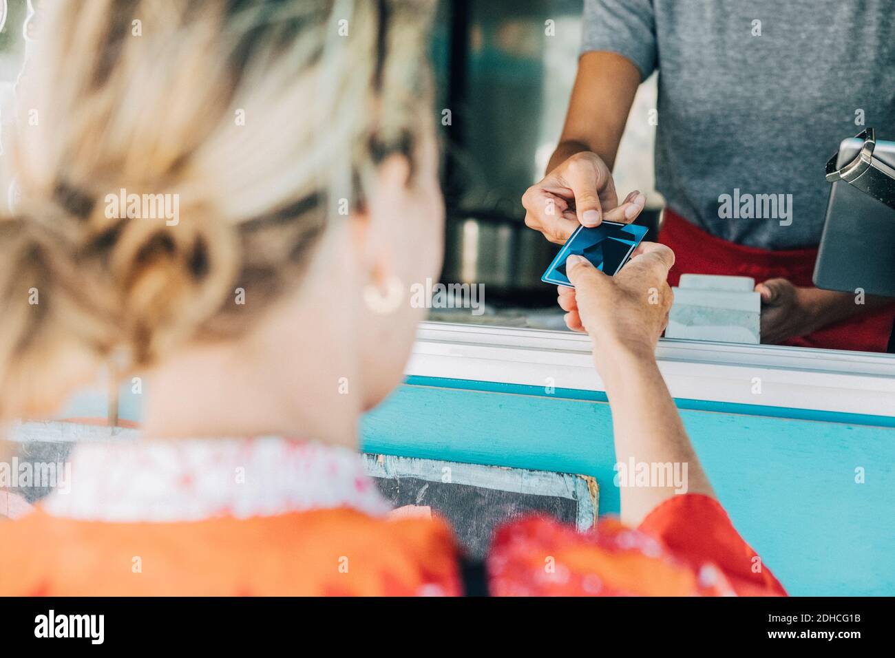 Rear view of female customer giving credit card to owner standing in ...