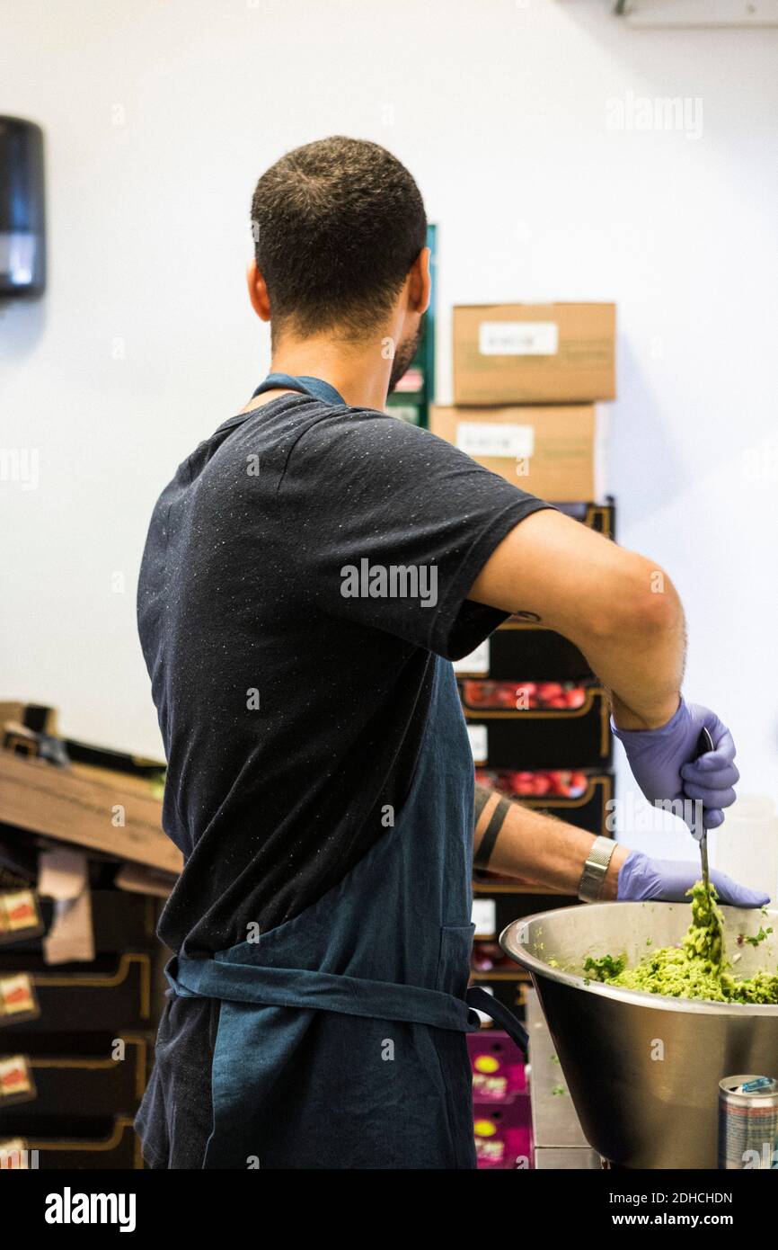Side view of young male chef preparing food in container at restaurant ...