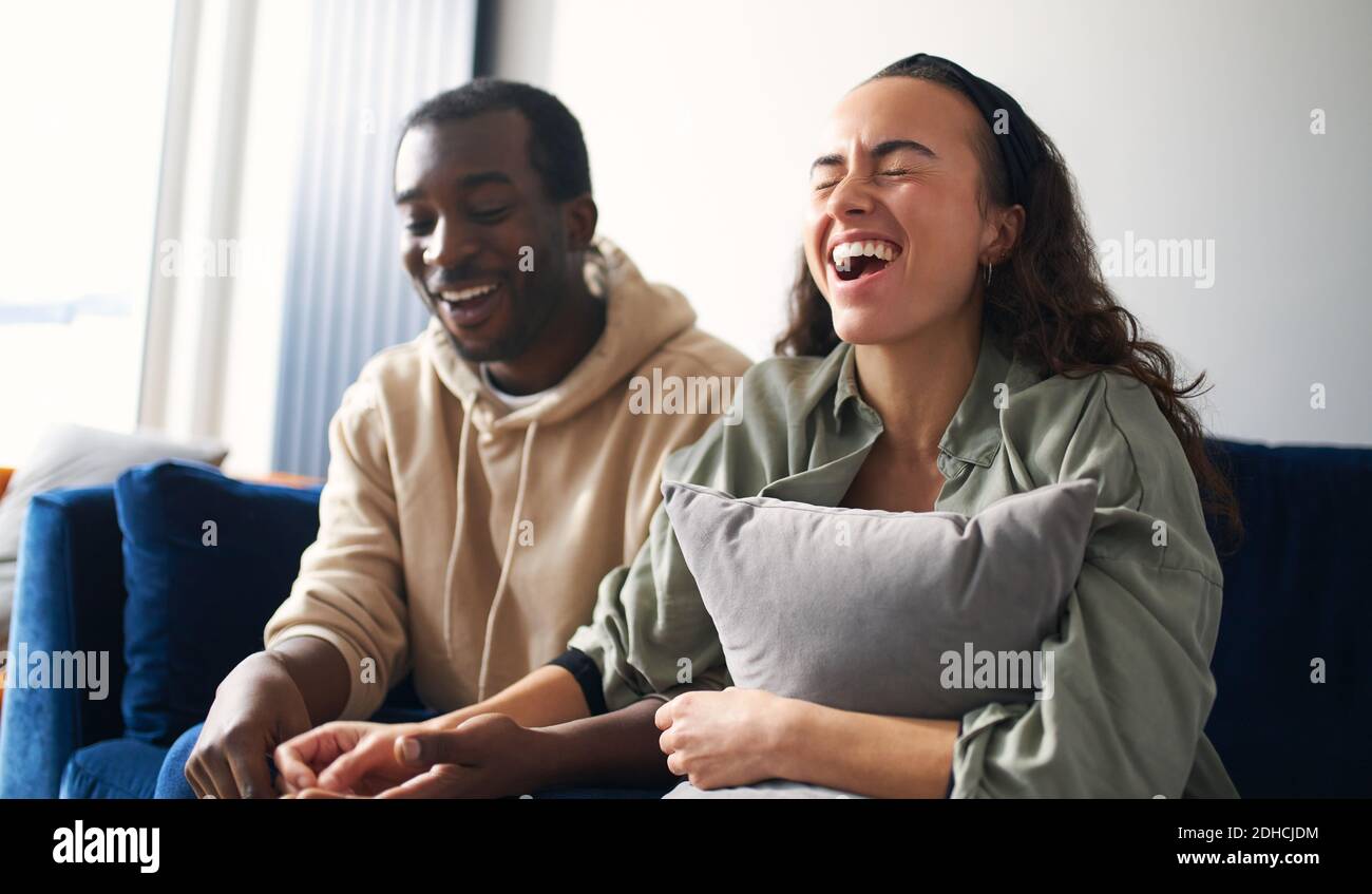Laughing young mixed ethnicity couple laughing whilst sitting on sofa ...