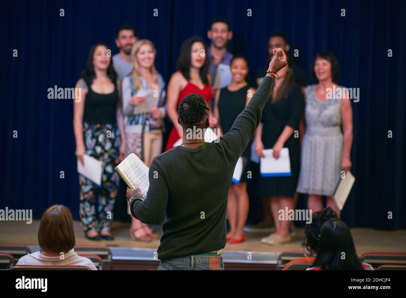 Male conductor with arm raised directing choir in auditorium Stock ...