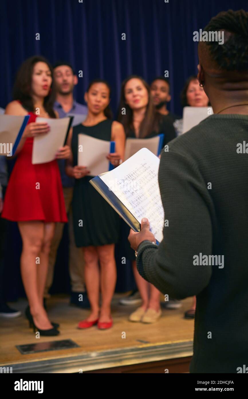 Male conductor holding music sheet directing choir on stage Stock Photo ...