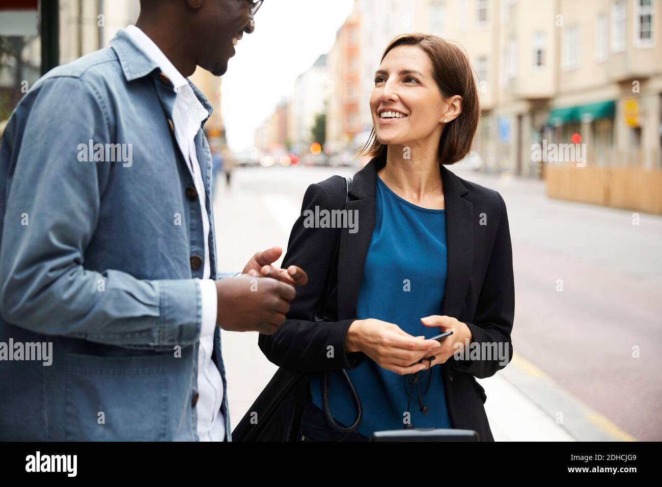 Smiling male and female commuters talking while standing on sidewalk in ...
