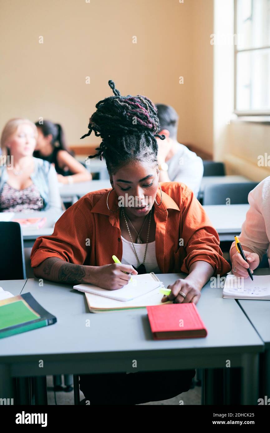 Confident young woman writing notes in classroom Stock Photo - Alamy