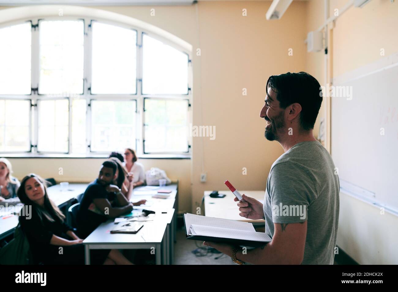 Happy teacher holding book and felt tip pen while teaching language to ...